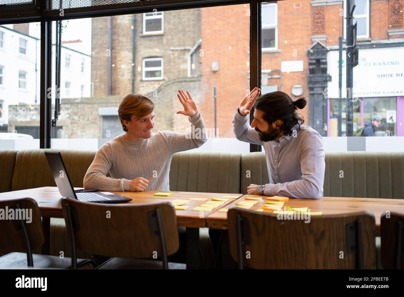 Male coworkers giving high five to each other while sitting at desk in ...