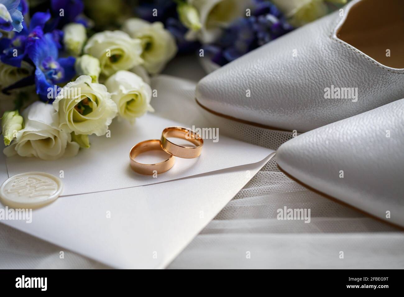 Wedding shoes for the bride. White high-heeled shoes near wedding rings ...