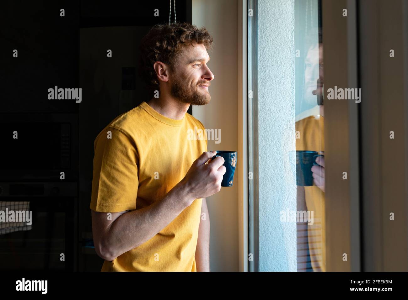 Smiling man looking through window while having coffee at home Stock ...