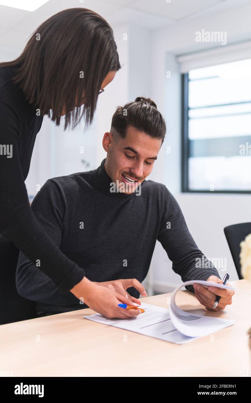 Female entrepreneur signing contract by male colleague at desk in ...