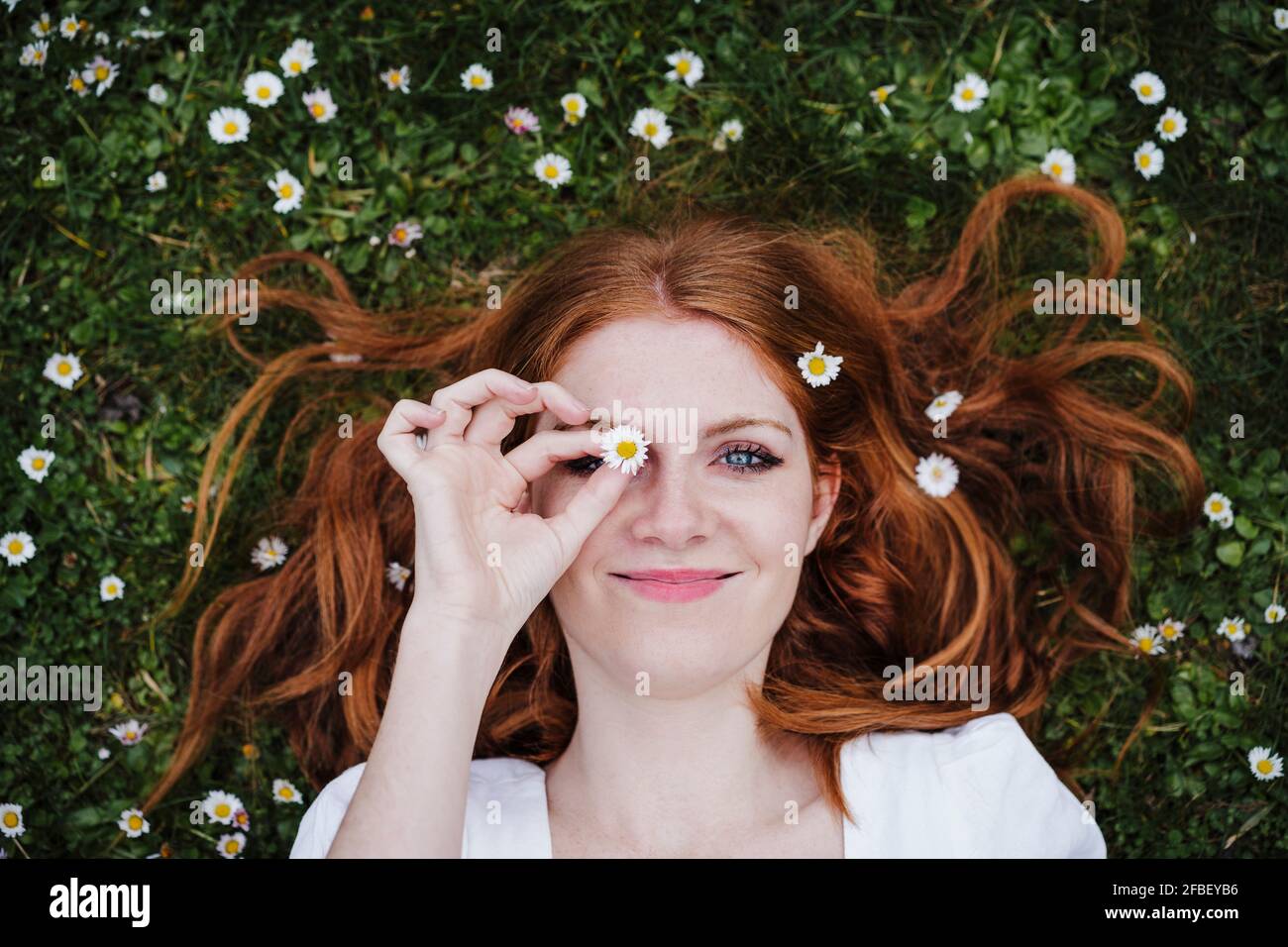 Smiling Beautiful Woman Covering Eye With Daisy Flower While Lying On
