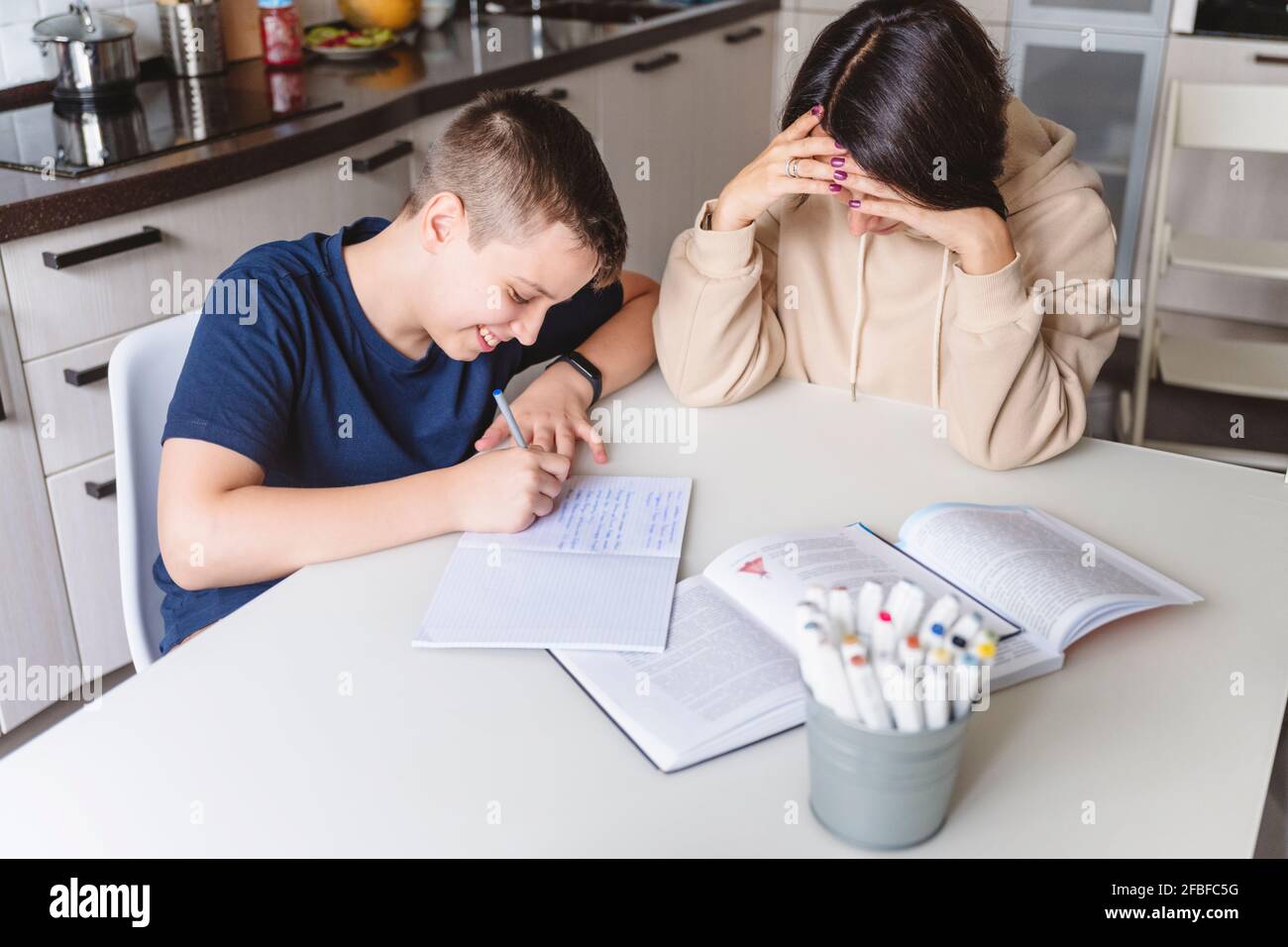 Frustrated mother helping son in completing homework while sitting on ...
