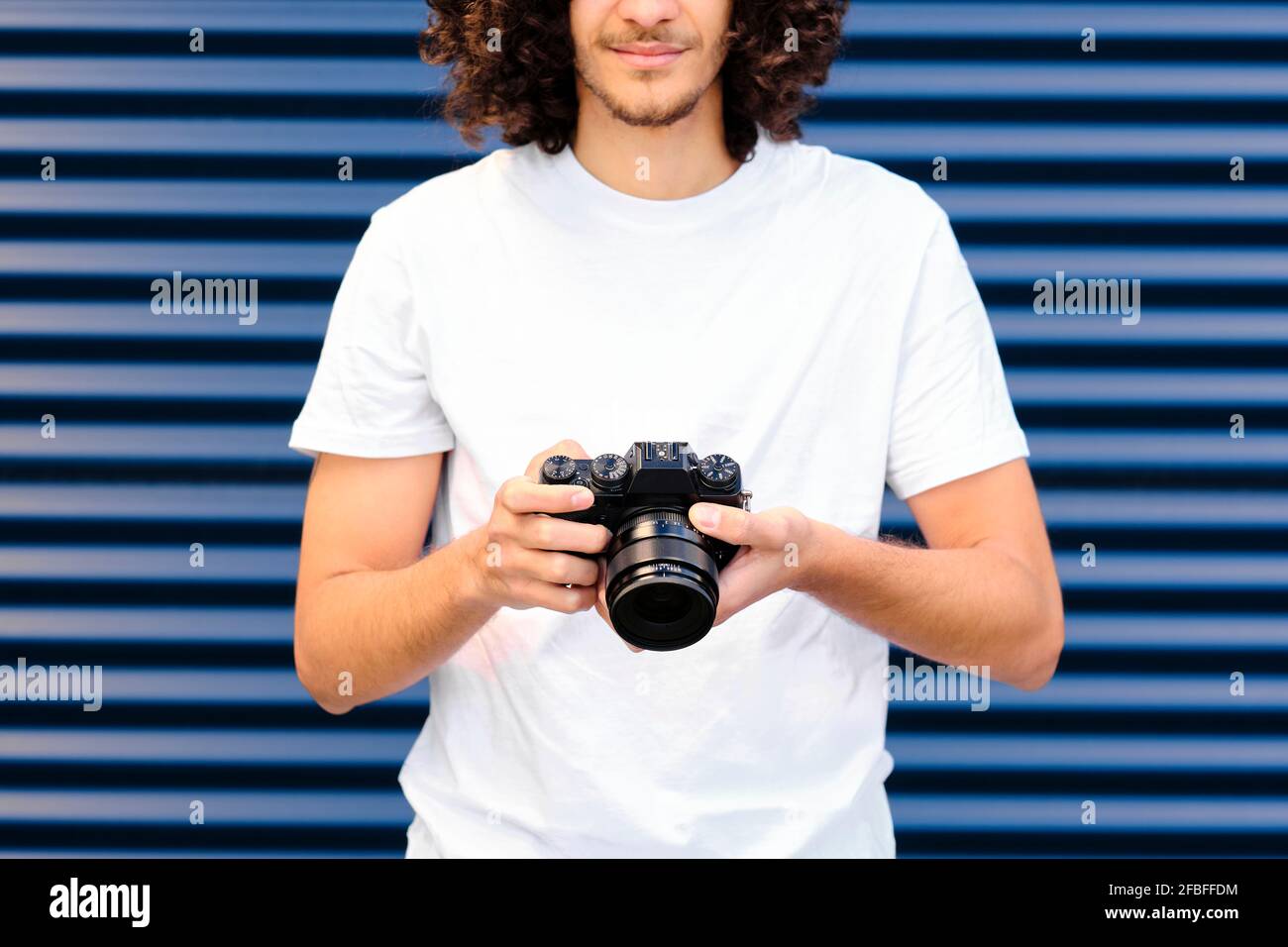 Young man holding camera while standing in front of closed shutter ...
