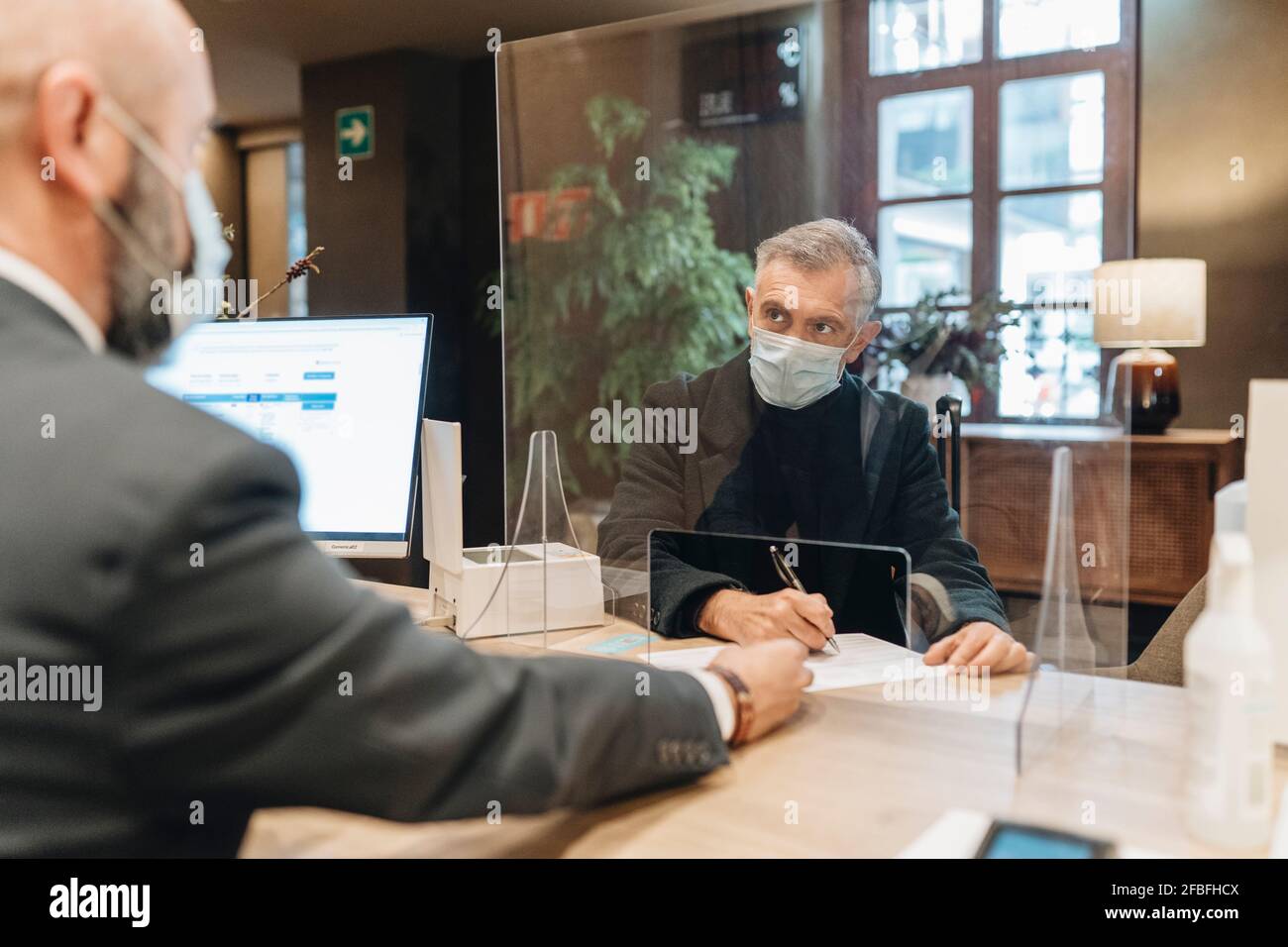 Man wearing protective face mask filling form at hotel reception Stock ...