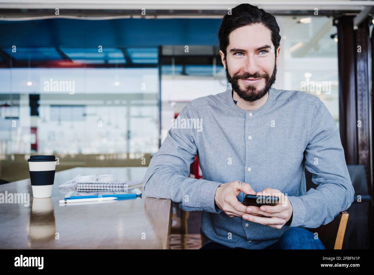 Smiling creative person holding mobile phone while looking away at work ...