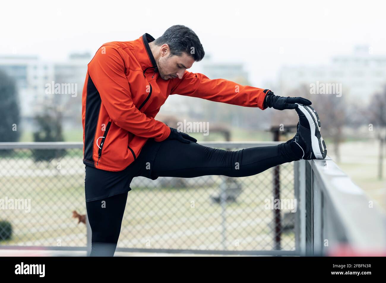 Male athlete touching toe while leg on chainlink fence at park Stock ...