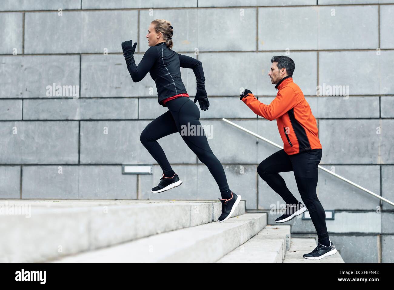 Athletic man and woman running up on steps by wall Stock Photo - Alamy