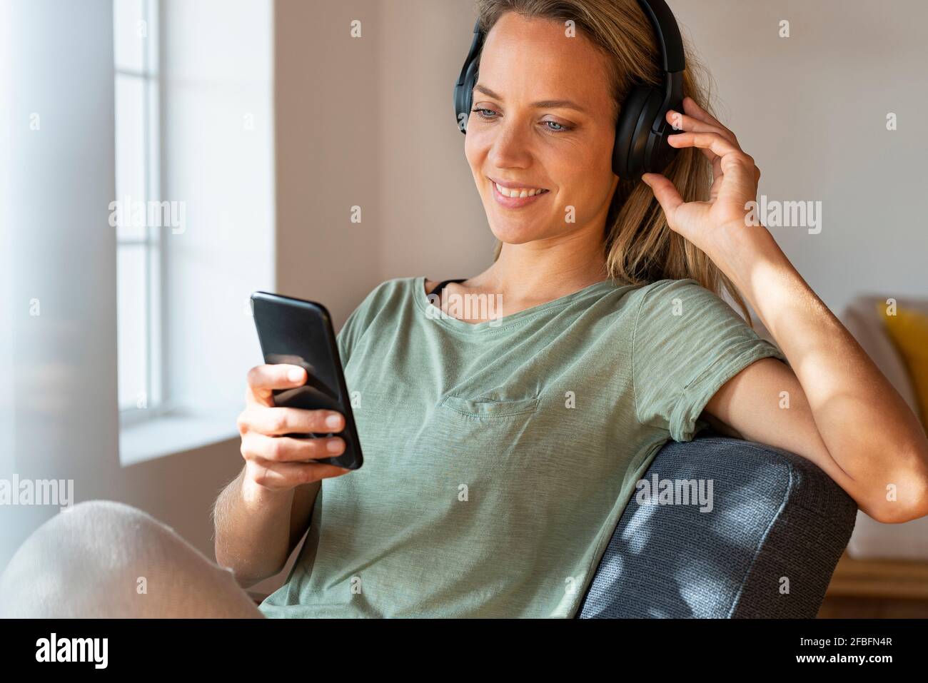 Smiling woman listening music through headphones while using mobile ...