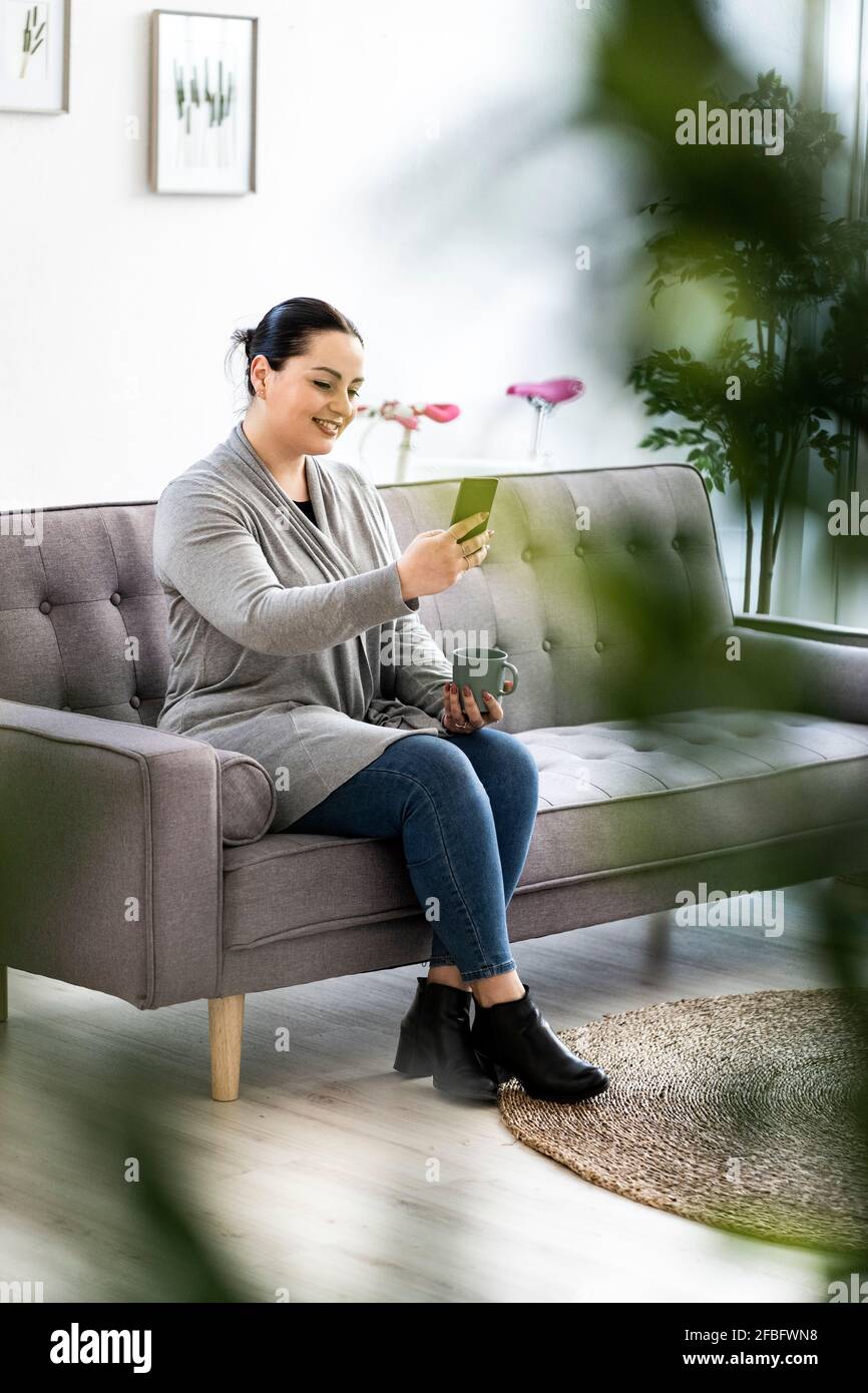 Smiling woman holding coffee mug while taking selfie through smart ...