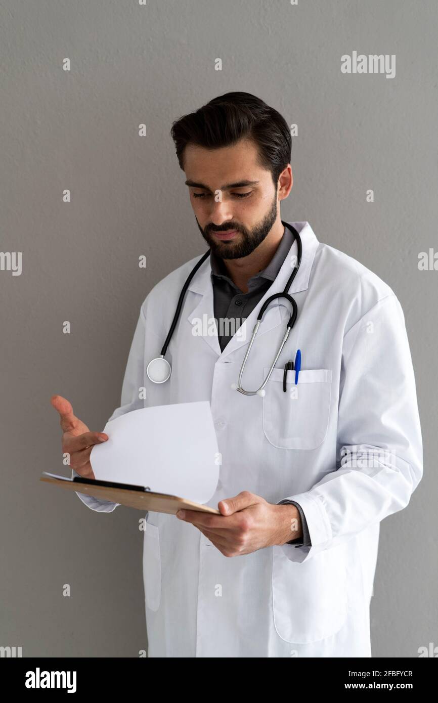 Male doctor reading medical report in front of wall Stock Photo - Alamy
