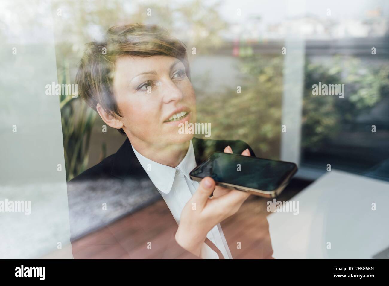 Contented businesswoman holding mobile phone while looking through ...