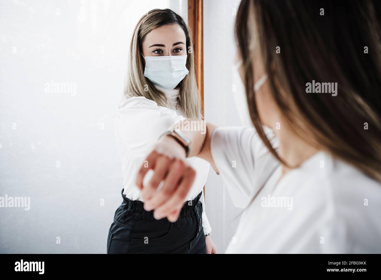 Female patient wearing protective face mask doing elbow bump with ...