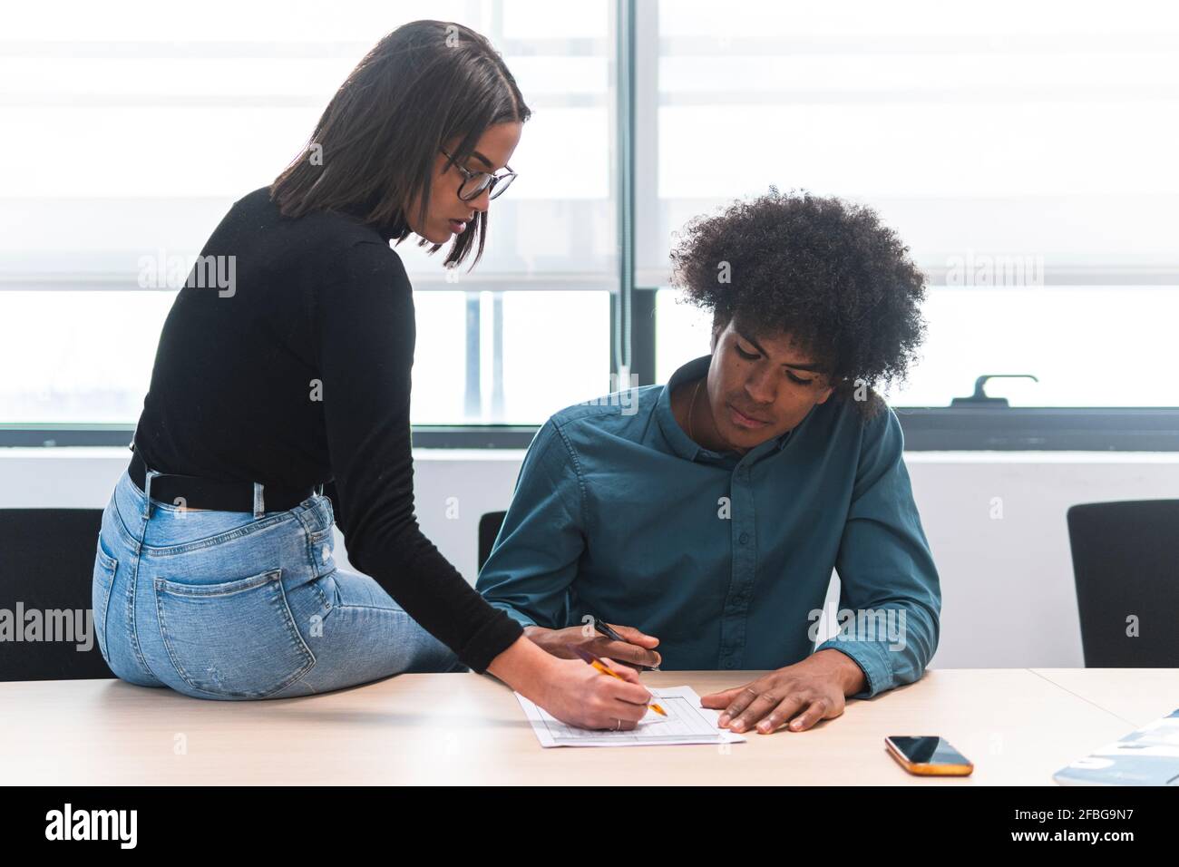 Female business professional assisting male colleague while working on ...