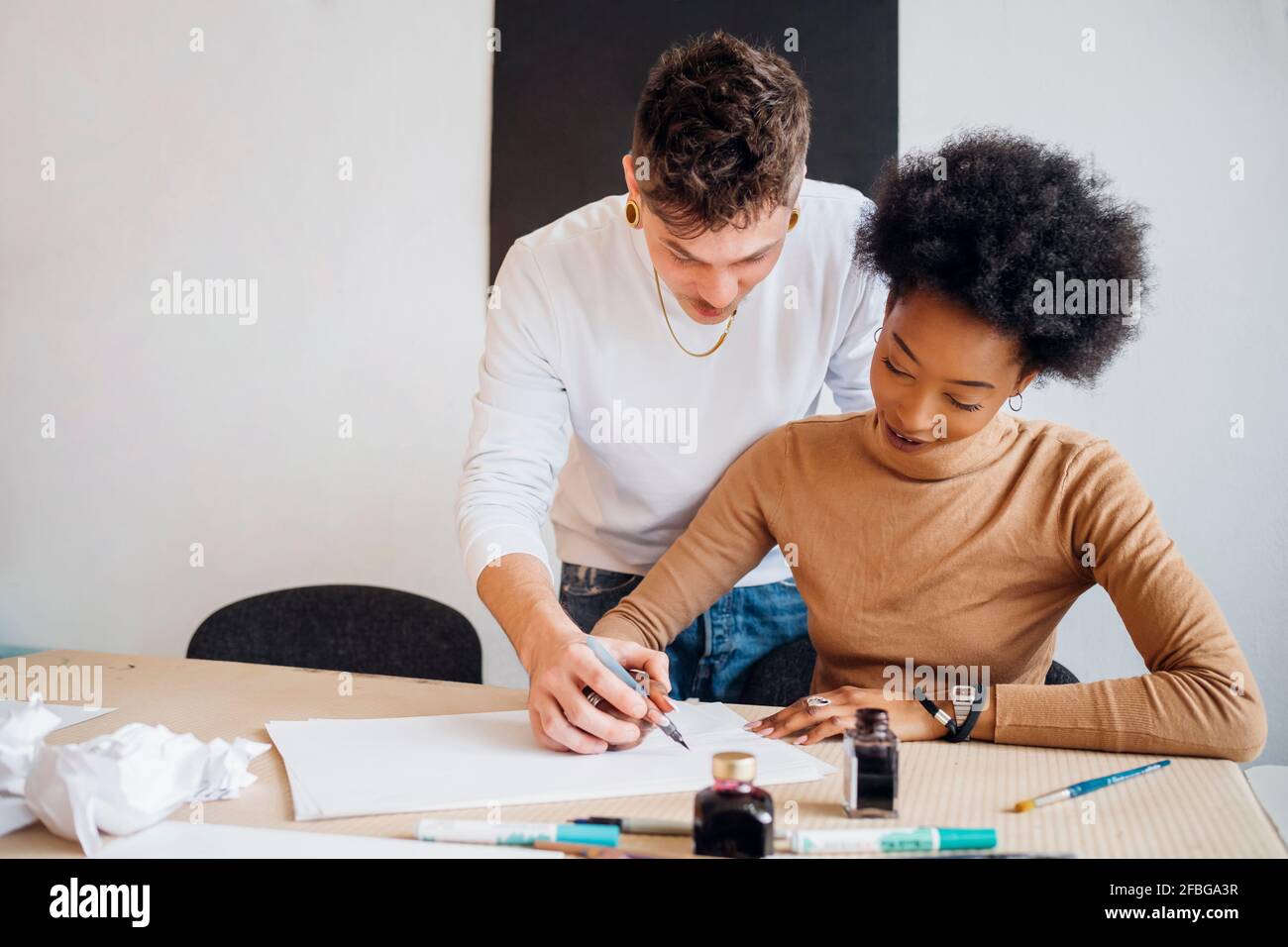 Young man helping girlfriend in practicing calligraphy in studio Stock ...