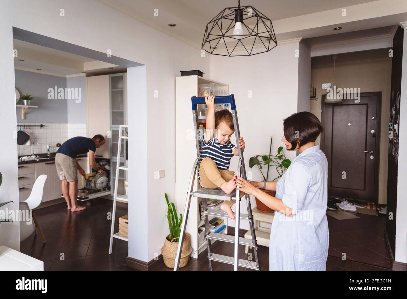 Mother playing with son sitting on ladder while father working in ...