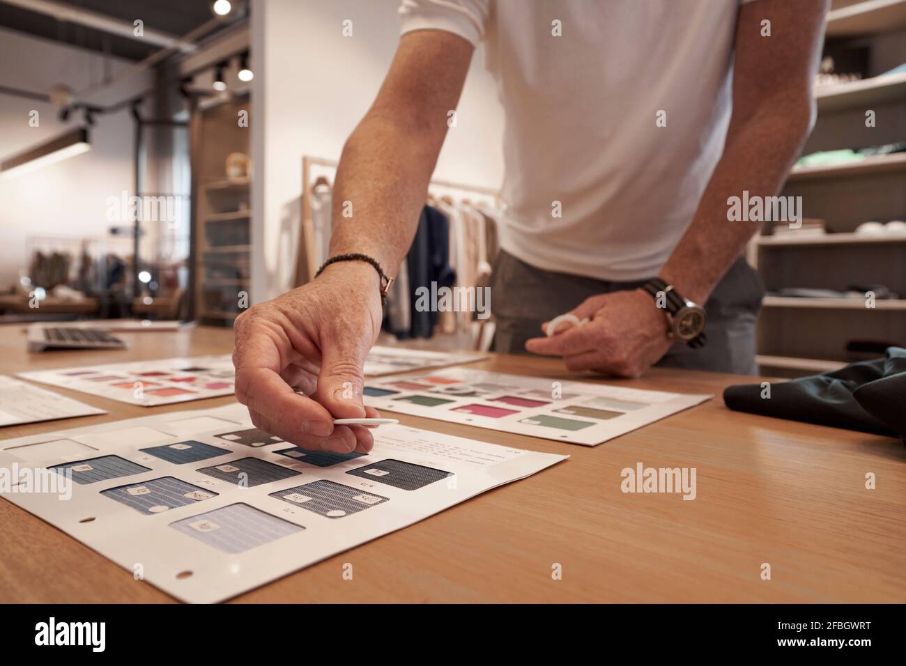 Male designer choosing fabric swatch from catalog at clothes design ...