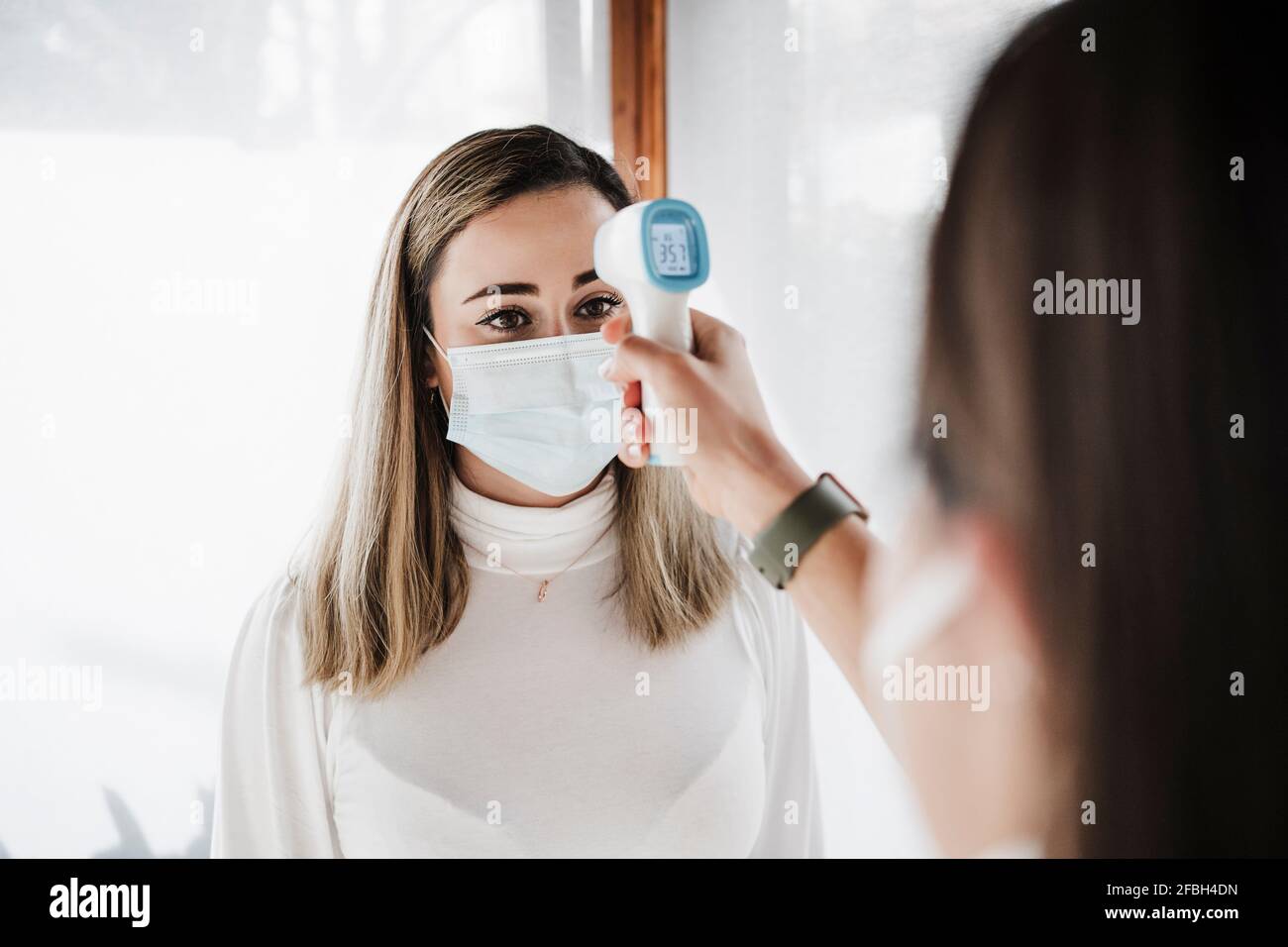 Female patient wearing protective face mask looking at doctor checking ...