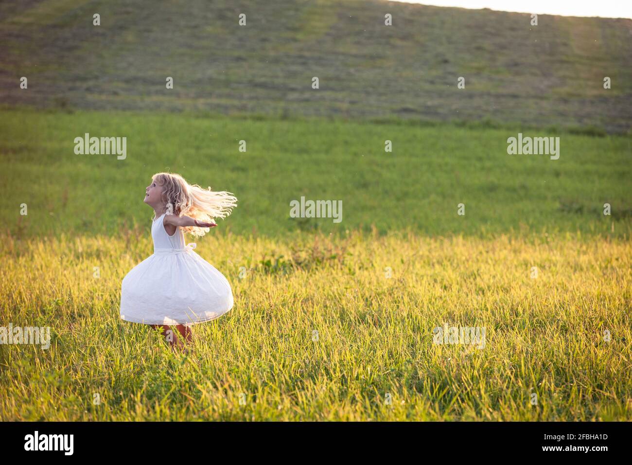 Girl with arms outstretched spinning on green grass during sunset Stock ...