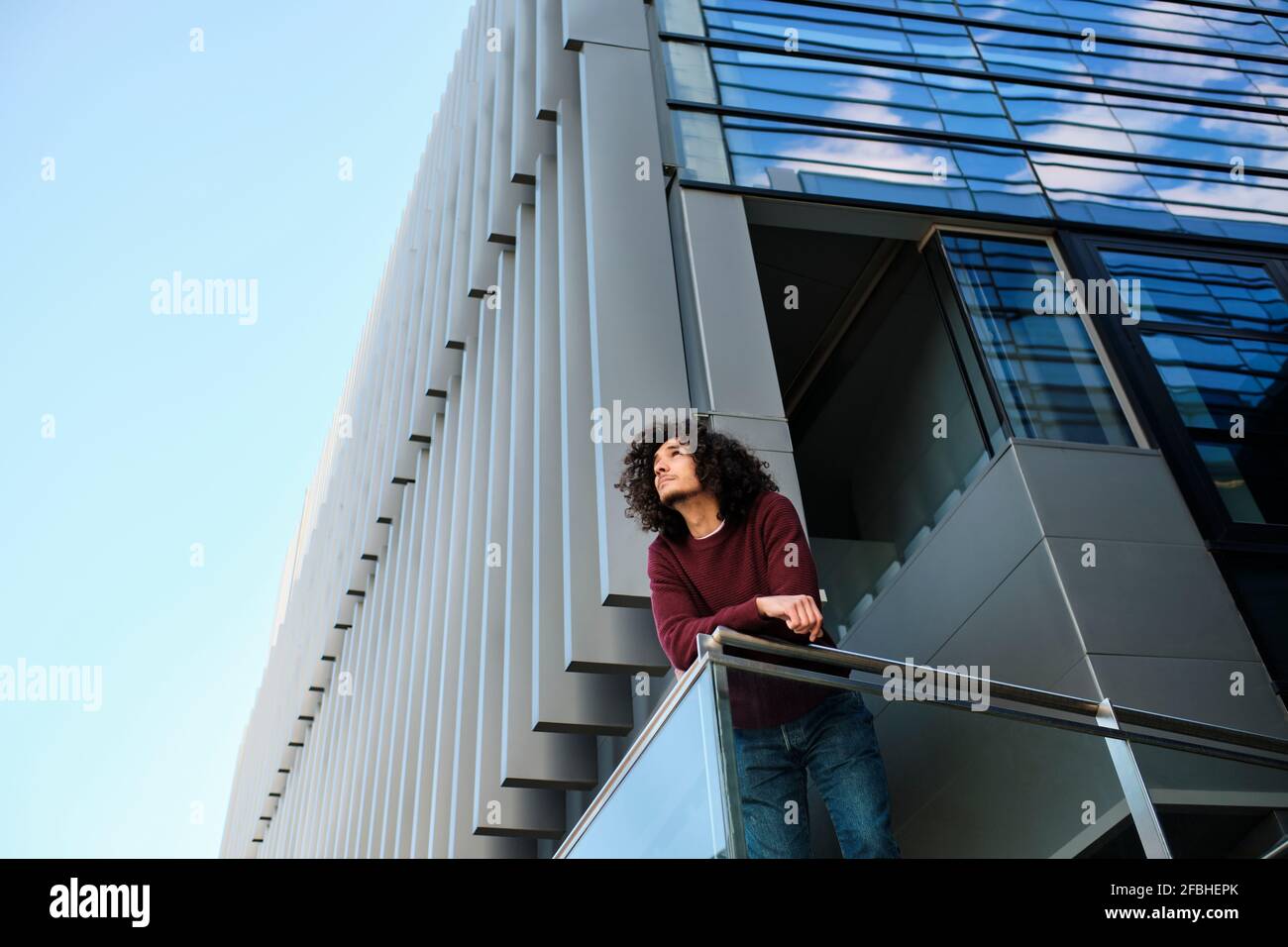 Young man leaning on railing while modern office building in background ...