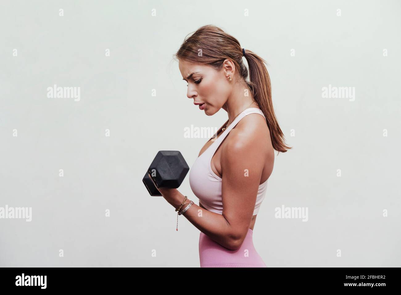 Female sportsperson lifting dumbbell while exercising by white wall ...