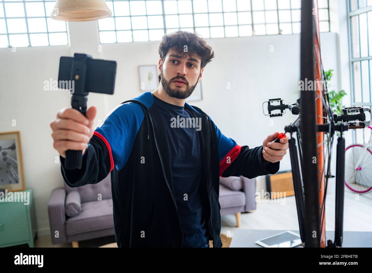 Male vlogger repairing bicycle while vlogging through smart phone at ...