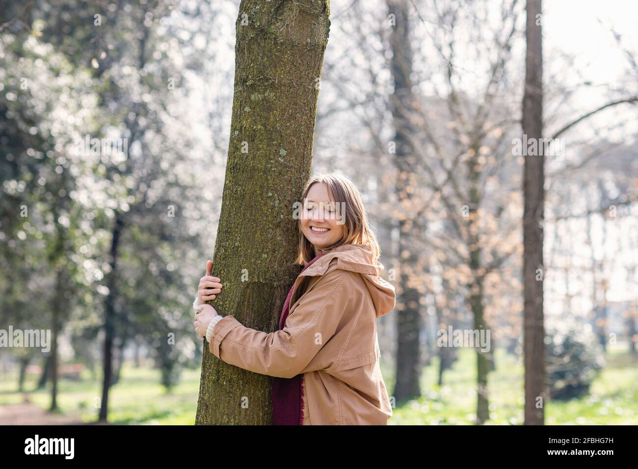 Happy mid adult woman hugging tree while standing at park Stock Photo ...