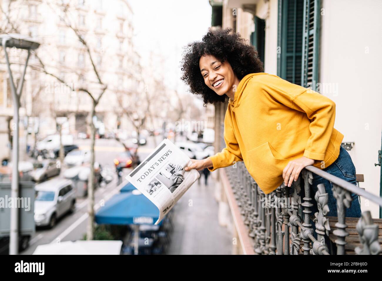 Cheerful young woman with newspaper leaning on railing in balcony Stock ...