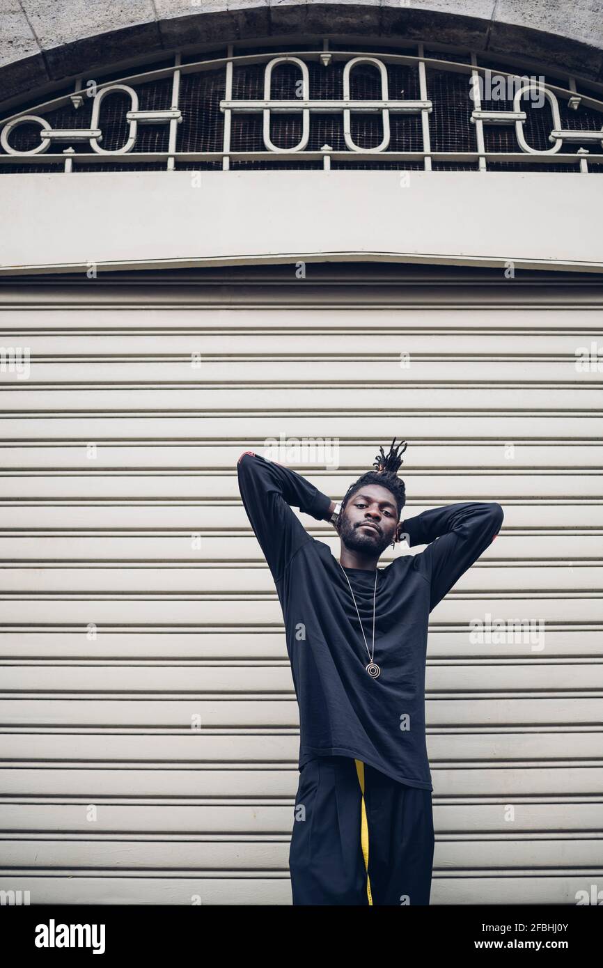 Young man standing with hands behind head against shutter Stock Photo ...