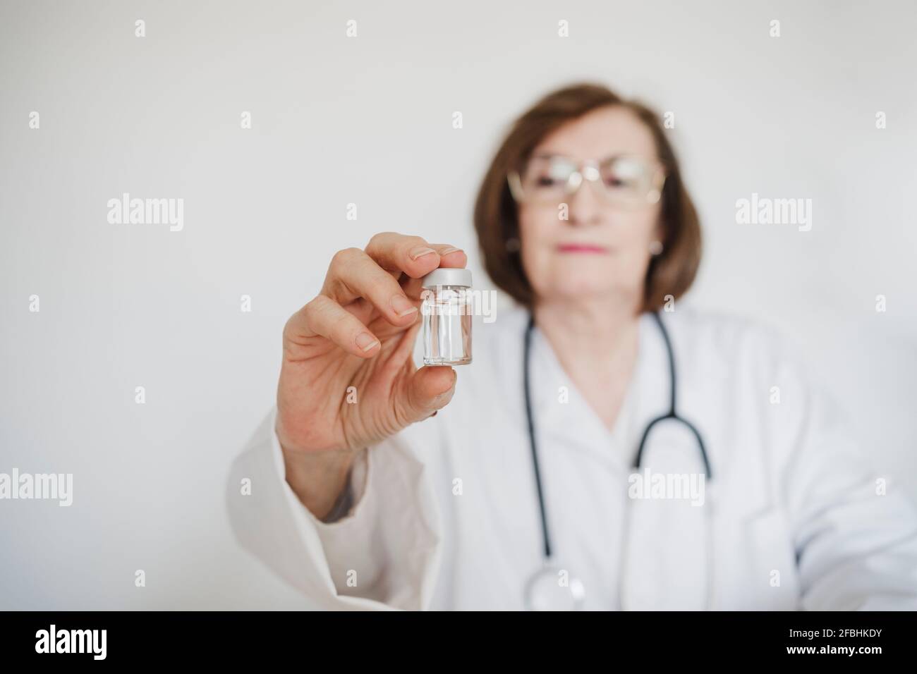 Senior female doctor holding vial in front of white wall Stock Photo ...