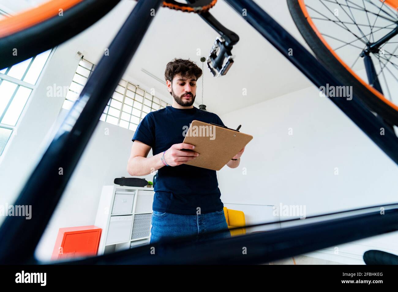 Young man writing notes while standing by upturnt bicycle at home Stock ...