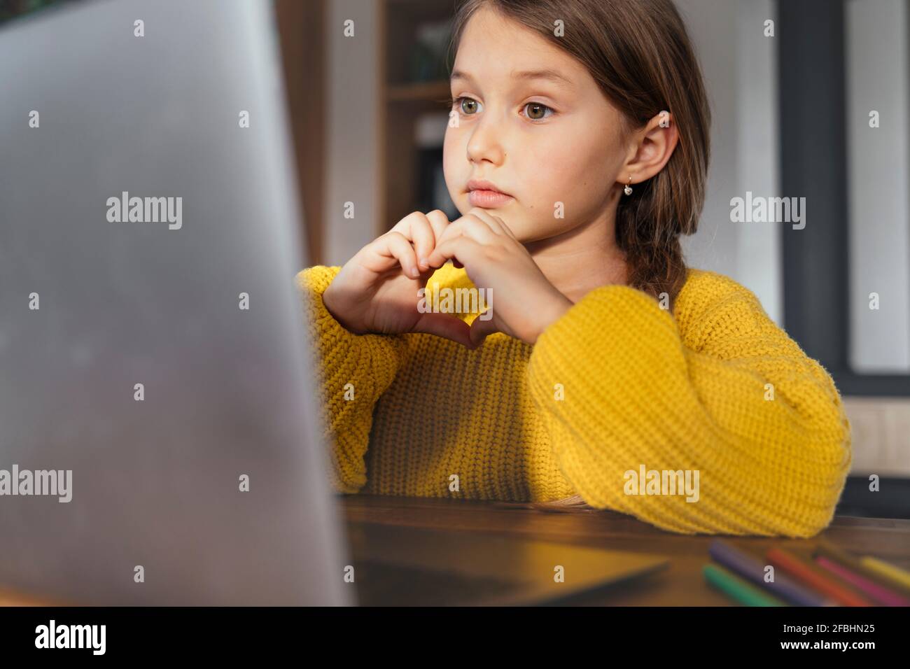 Cute little girl making heart shape with hand during video call on ...