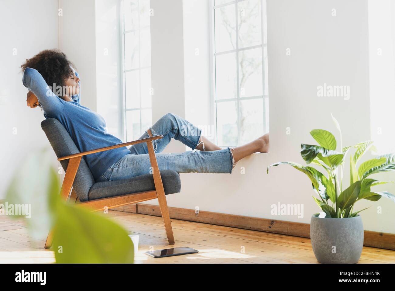 Young woman sitting with hands behind head on armchair at home Stock ...