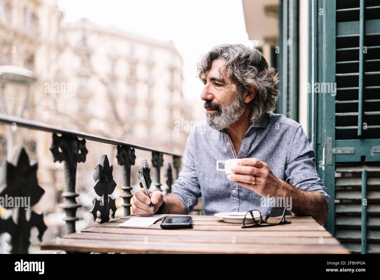 Senior man having coffee writing in note pad while looking away in ...