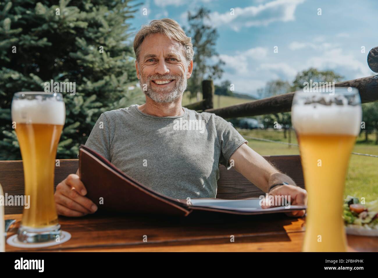 Smiling bearded man holding menu while sitting in beer garden Stock ...
