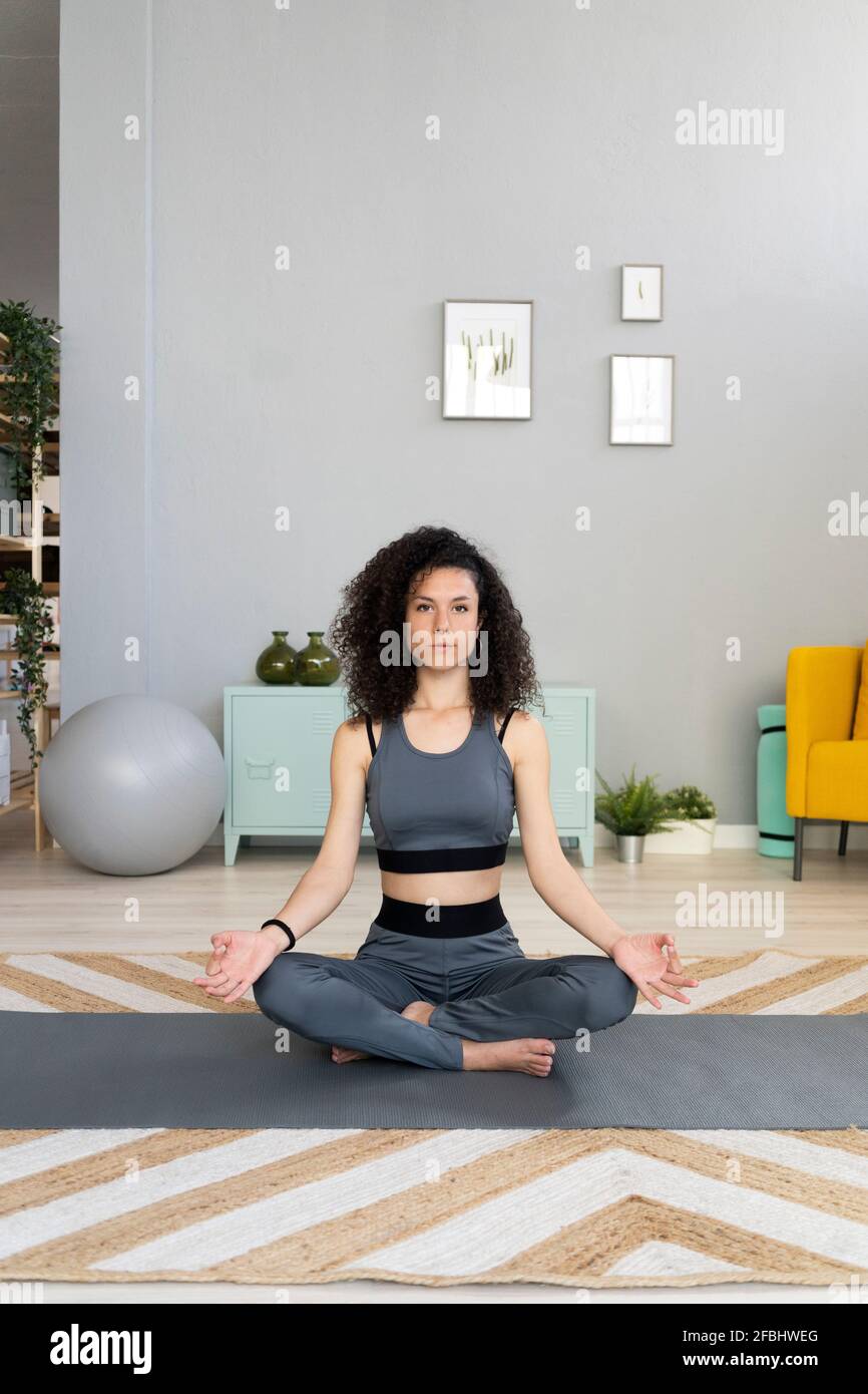 Young woman practicing lotus position on exercise mat in living room ...