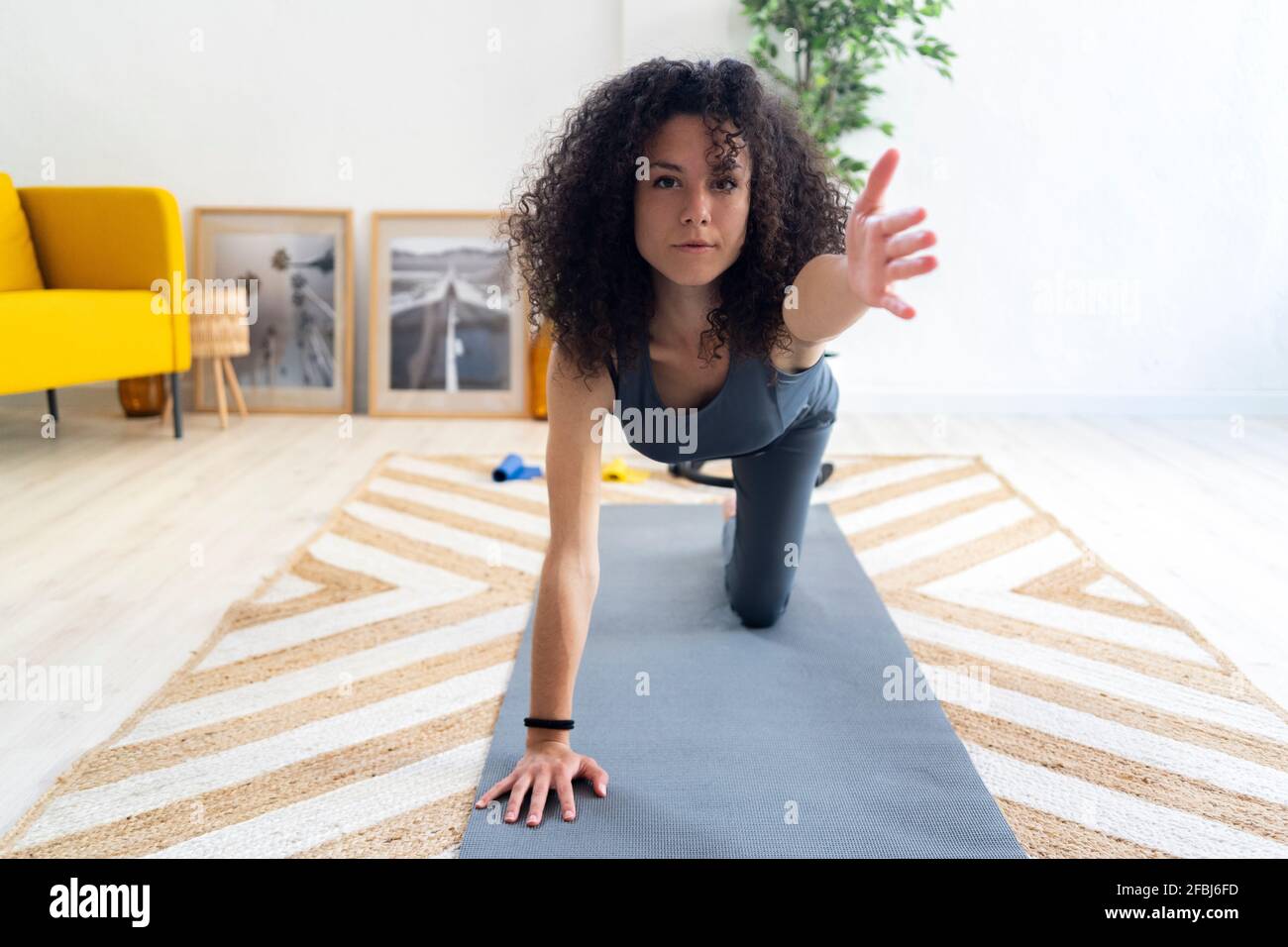 Curly haired woman stretching hand while exercising in living room ...