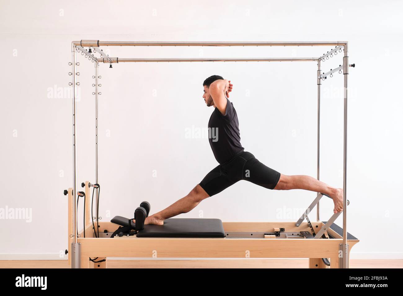 Male athlete with hands behind head practicing pilates on cadillac ...
