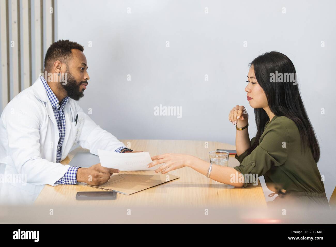 Male doctor holding paper while explaining patient at clinic Stock ...