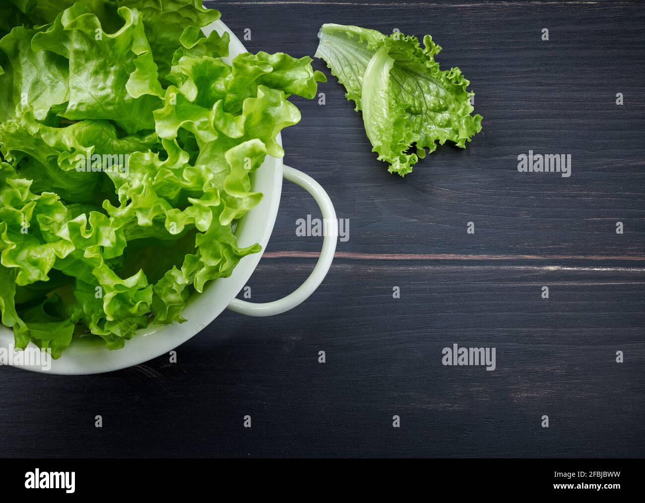 fresh green lettuce leaves in white colander on dark wooden kitchen ...