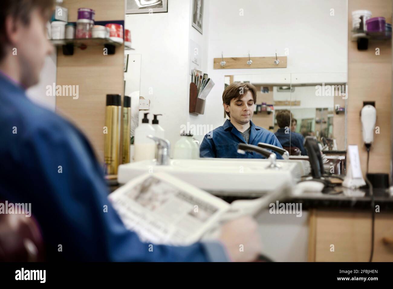 Reflection of barber reading newspaper in barber shop Stock Photo - Alamy