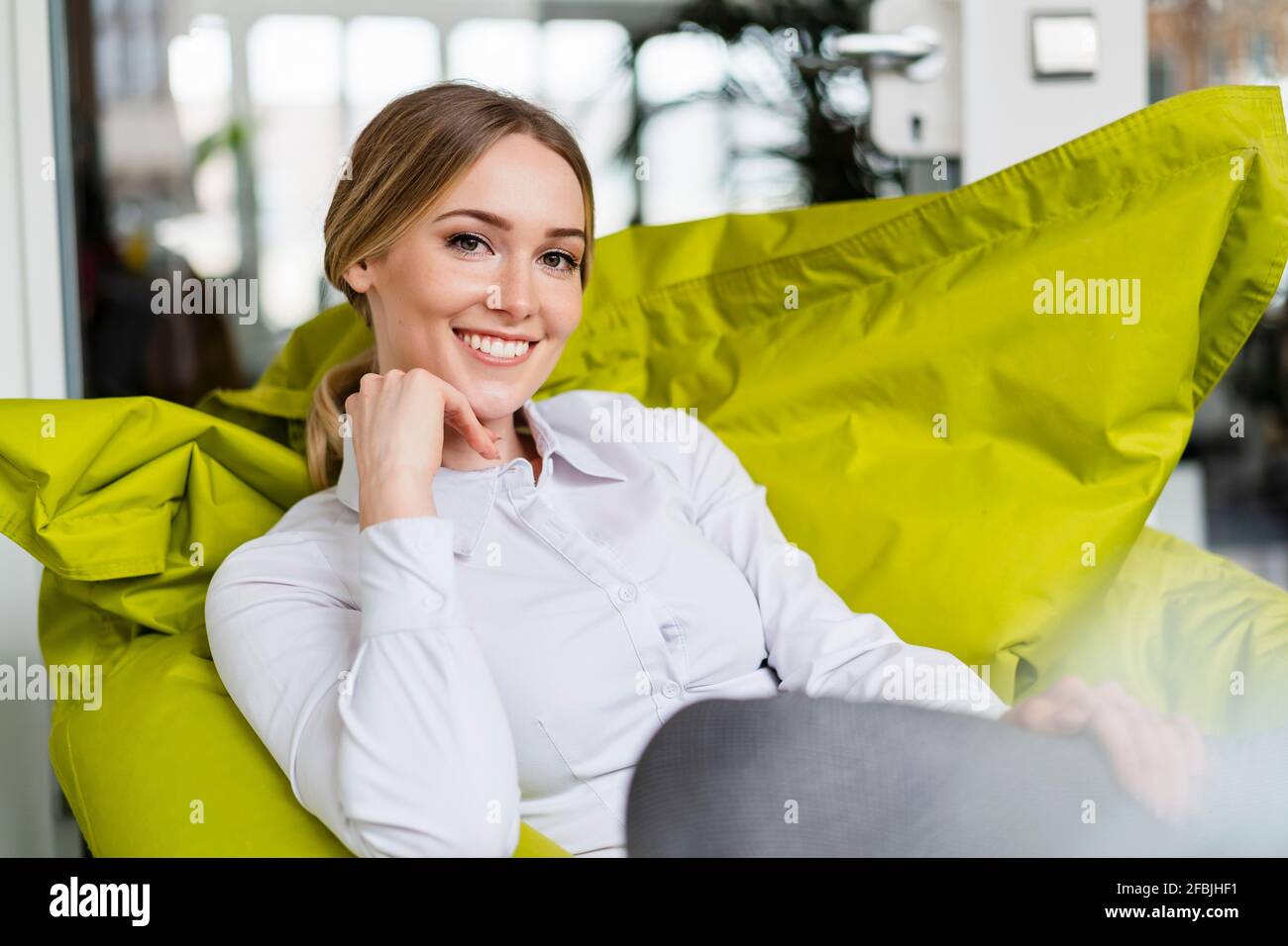 Contented businesswoman with hand on chin sitting on bean bag at office ...