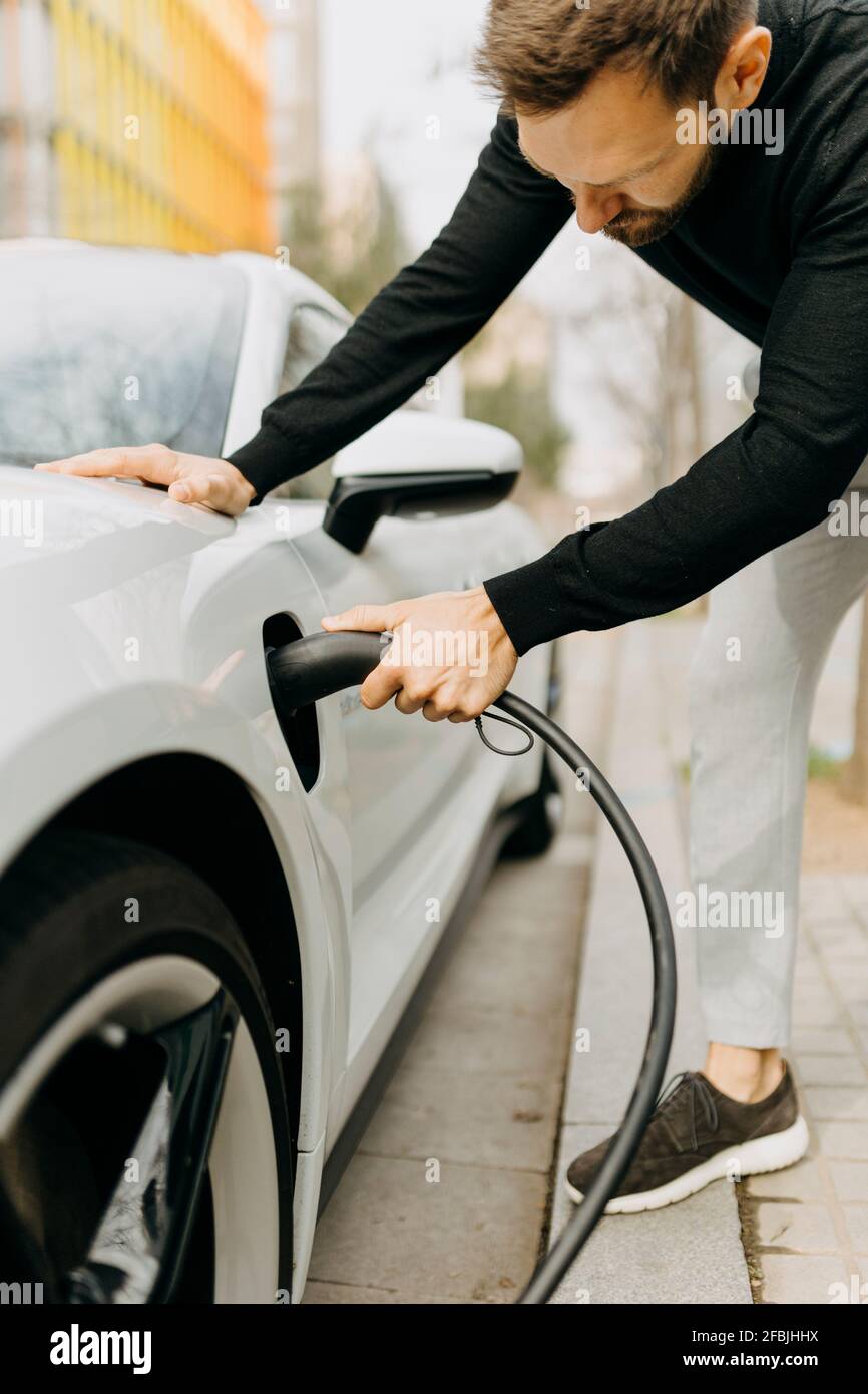 Man plugging electric cord in car at charging station Stock Photo - Alamy