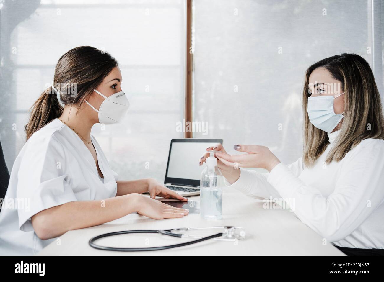 Patient taking sanitiser while talking with female doctor at desk in ...