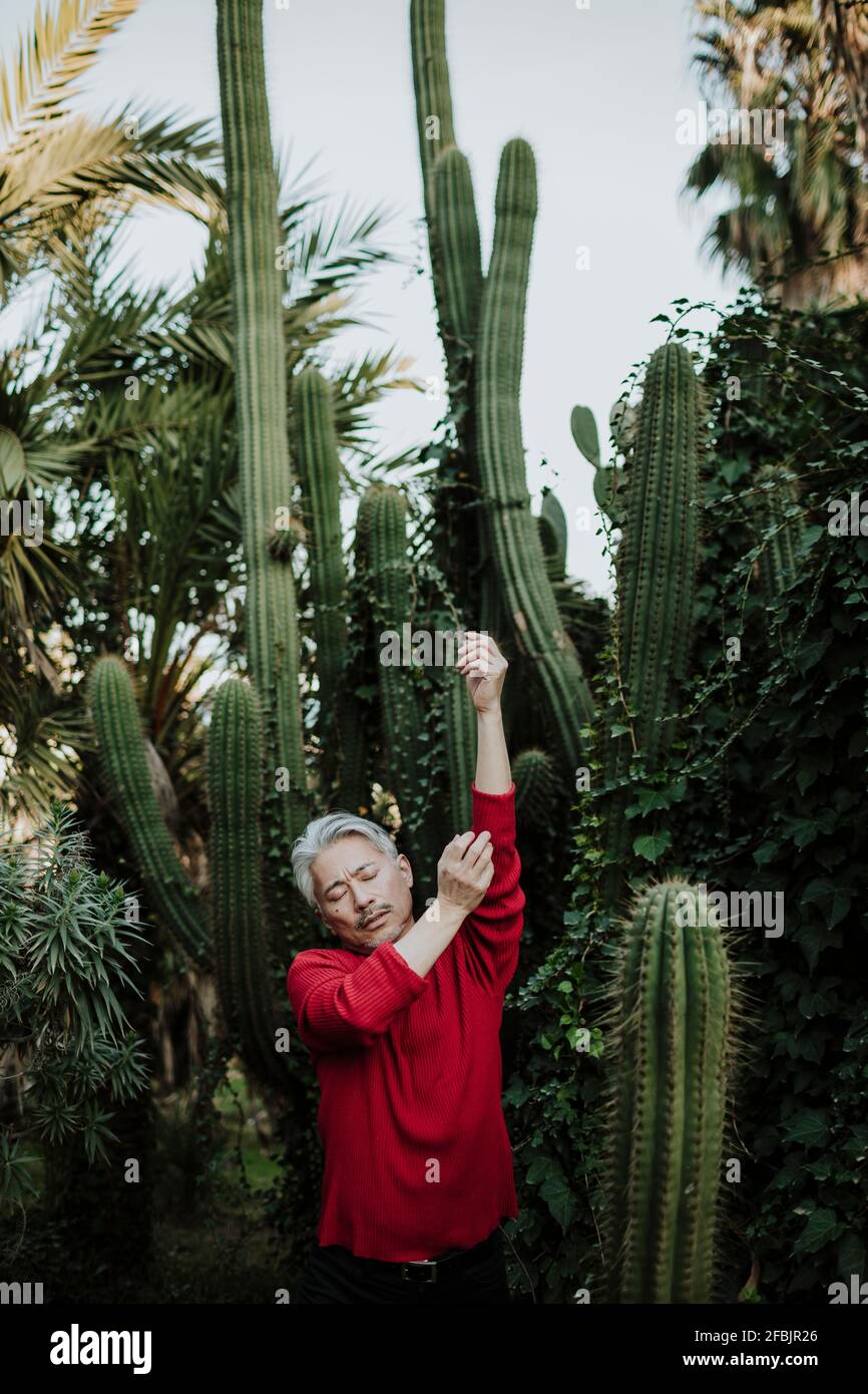 Mature man hugging self while standing in cactus garden Stock Photo - Alamy
