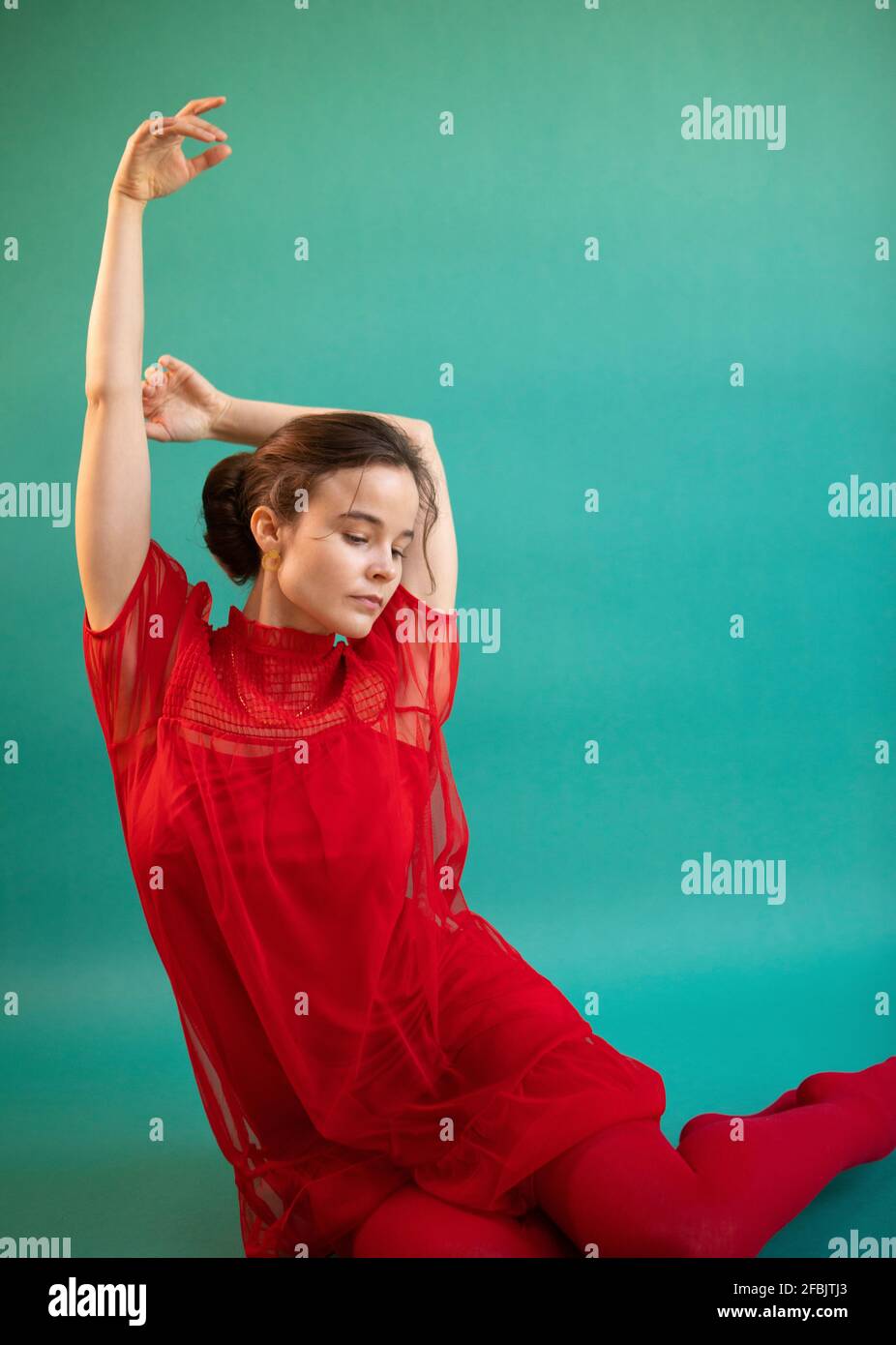 Young woman ballet dancer with arms raised sitting over turquoise floor ...