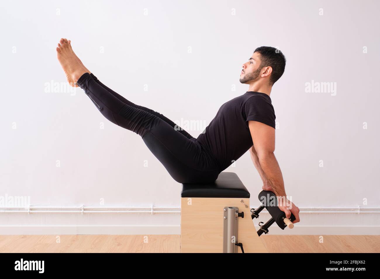 Concentrated man practicing pilates on chair by wall in exercise room ...