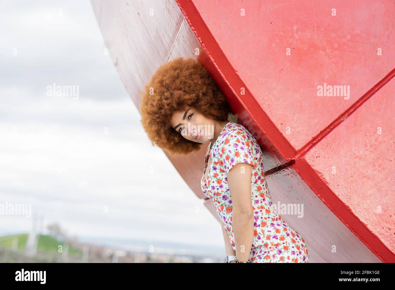 Redhead young woman standing by red curve wall Stock Photo - Alamy