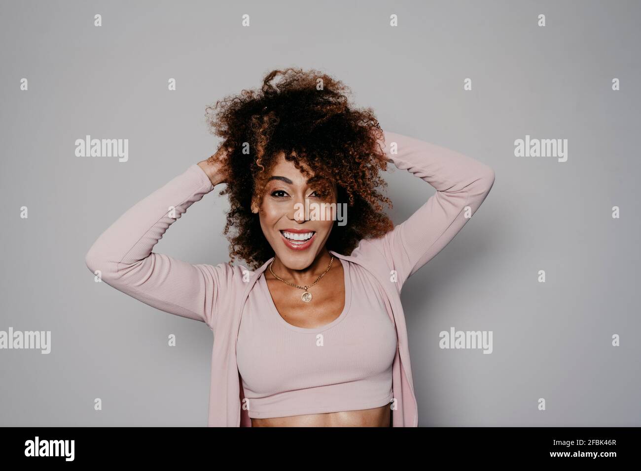 Cheerful young woman with hands in hair against gray background Stock ...