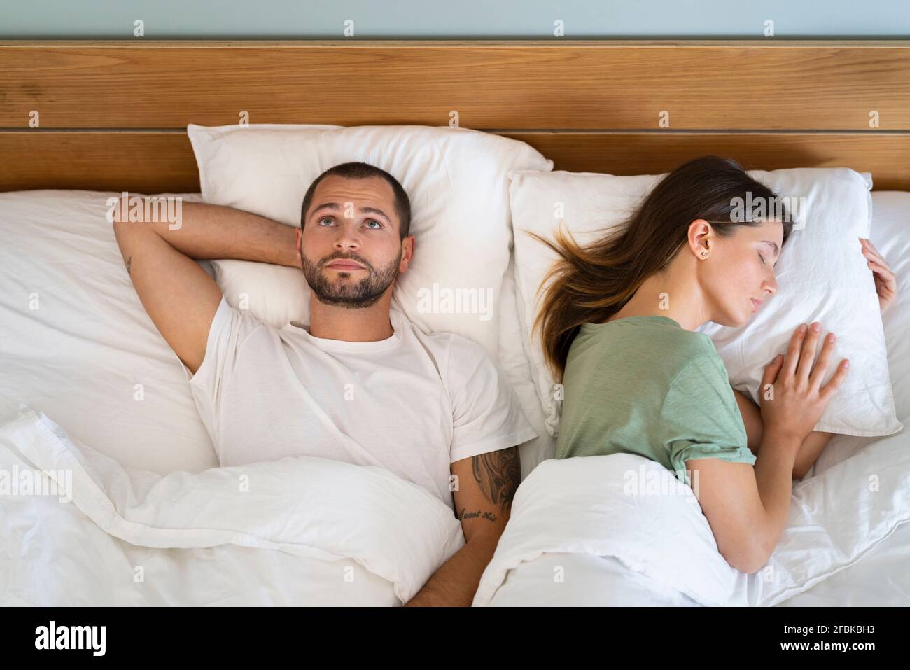 Young woman sleeping by worried man staring at ceiling while lying on ...