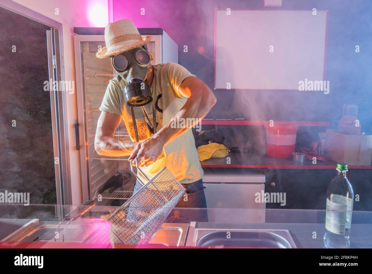 Mature man in gas mask preparing food in deep fryer at commercial ...